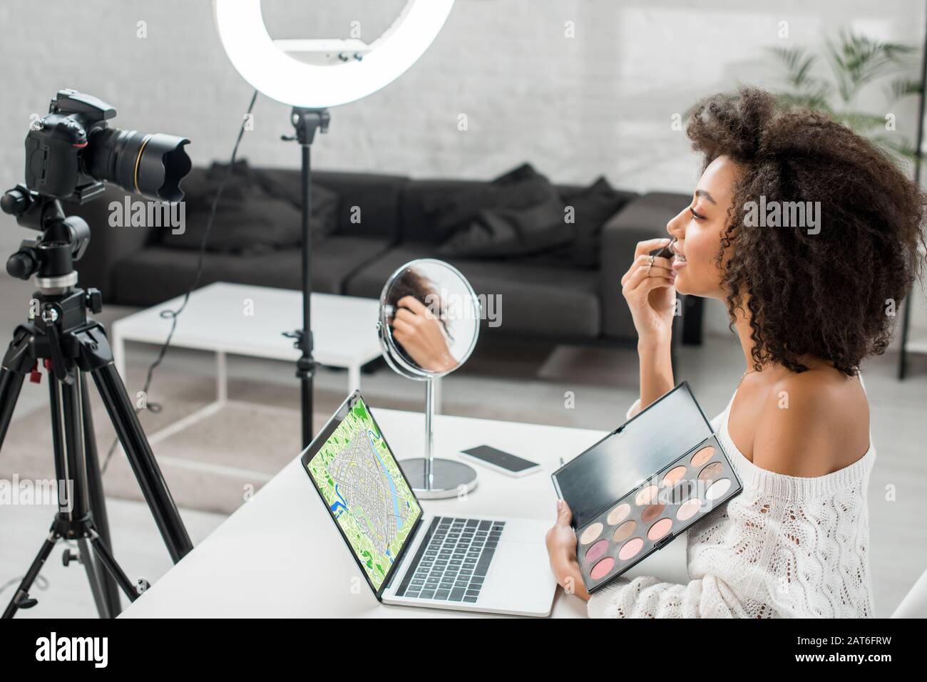 side view of happy african american influencer holding eye shadow ...