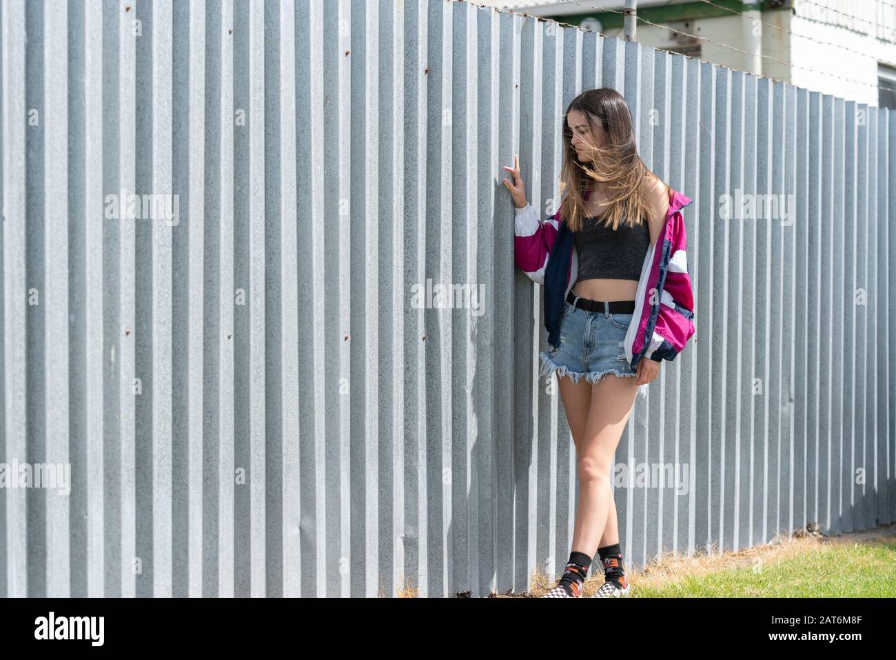 Modern teenage girl standing by corrugated iron fence background with ...