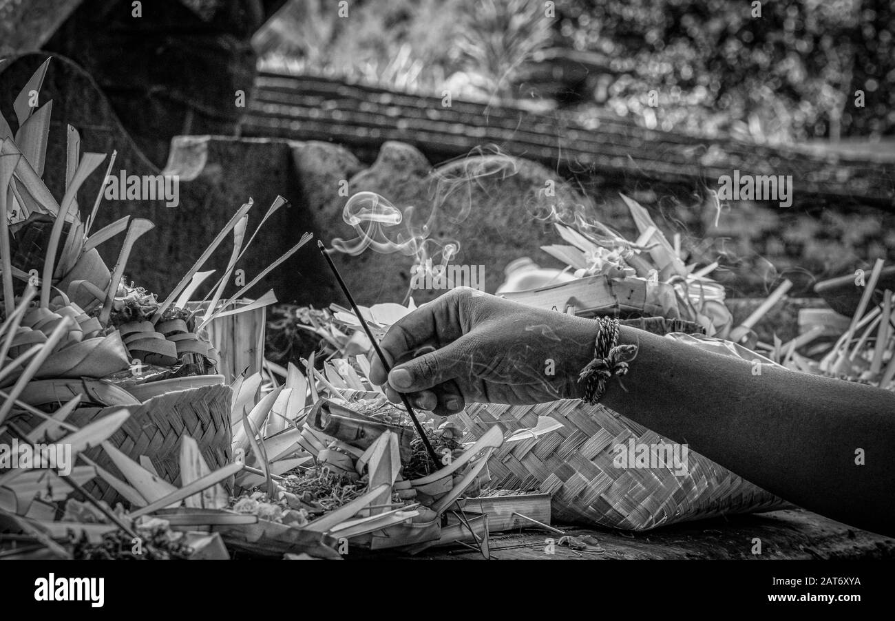 A hand placing burning incense in an offering at a Balinese temple ...