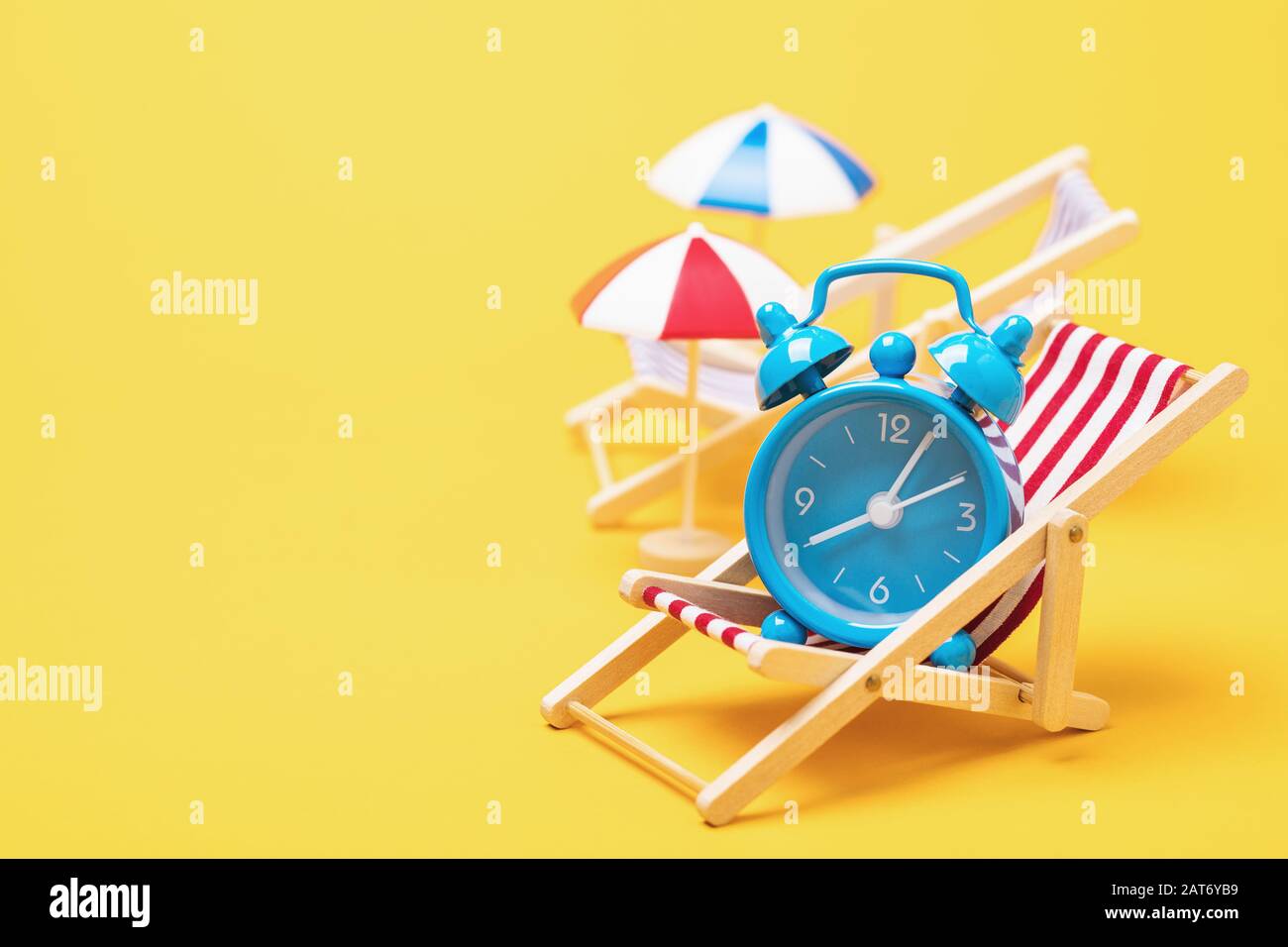 Alarm clock in a deck chair with a parasol on a yellow background with ...