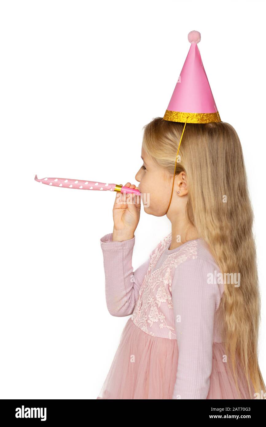 Small child in pink hat blowing in birthday pipe on white background ...