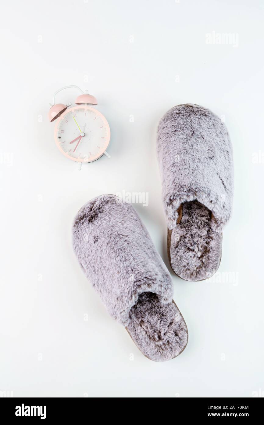 Flat lay with Soft fluffy slippers gray color and pink alarm clock ...