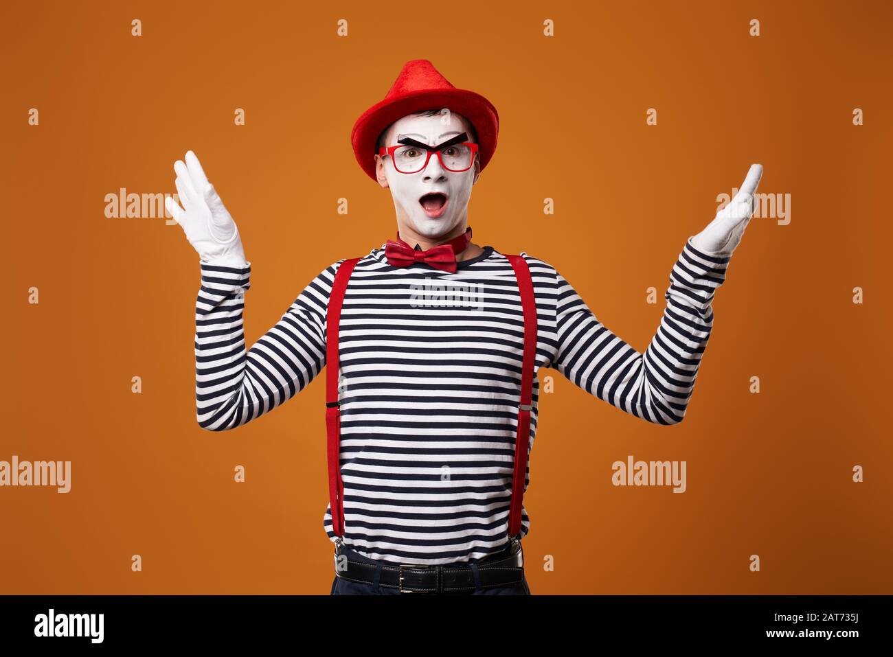 Surprised mime in red hat and vest showing thumb up on empty orange ...