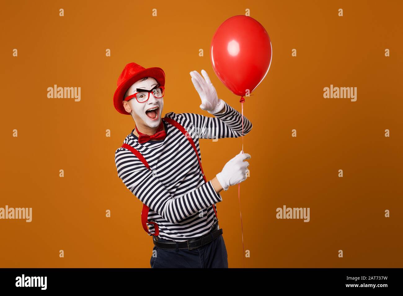 Mime man in vest and red hat with balloon in his hand on orange empty ...