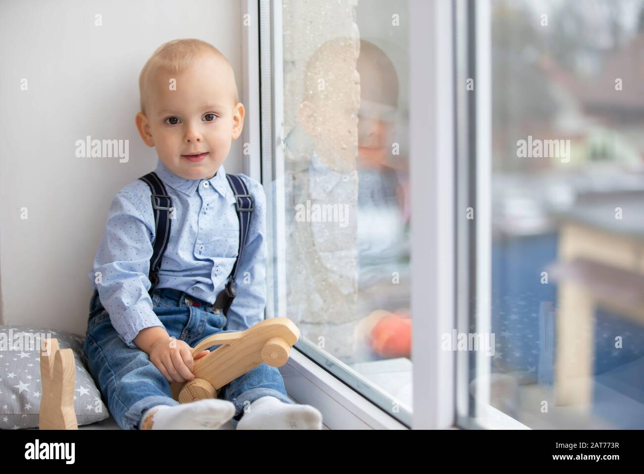 Little baby near the window. The kid with a toy sits on a window sill ...
