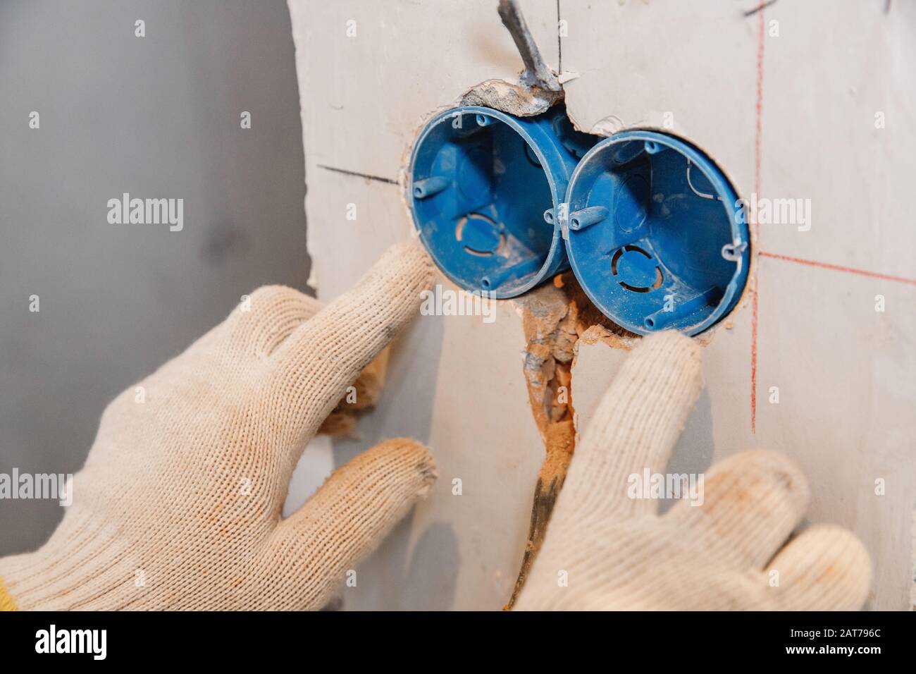 Builder worker installs plastic box under electrical outlet in hole ...