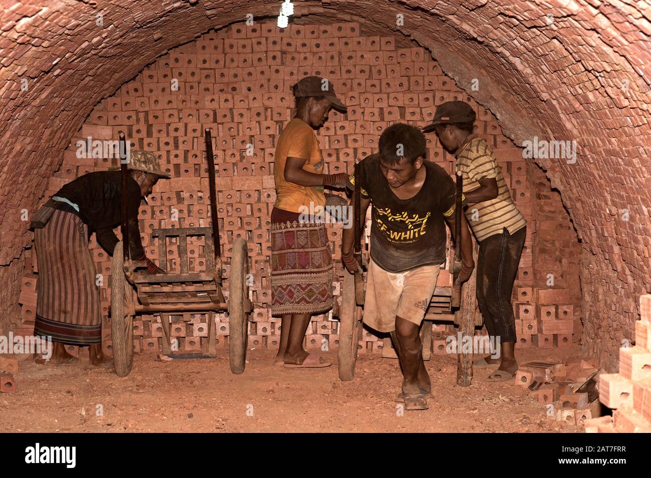 Workers transport fired bricks inside a ring kiln of a brick factory ...