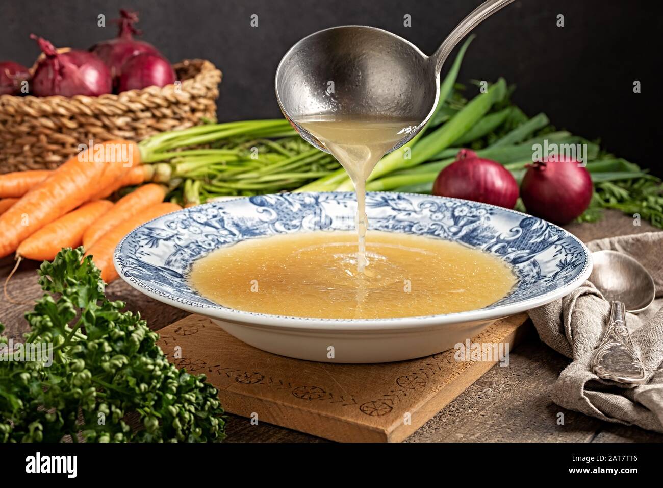 Pouring chicken bone broth from a ladle into a vintage plate, with ...