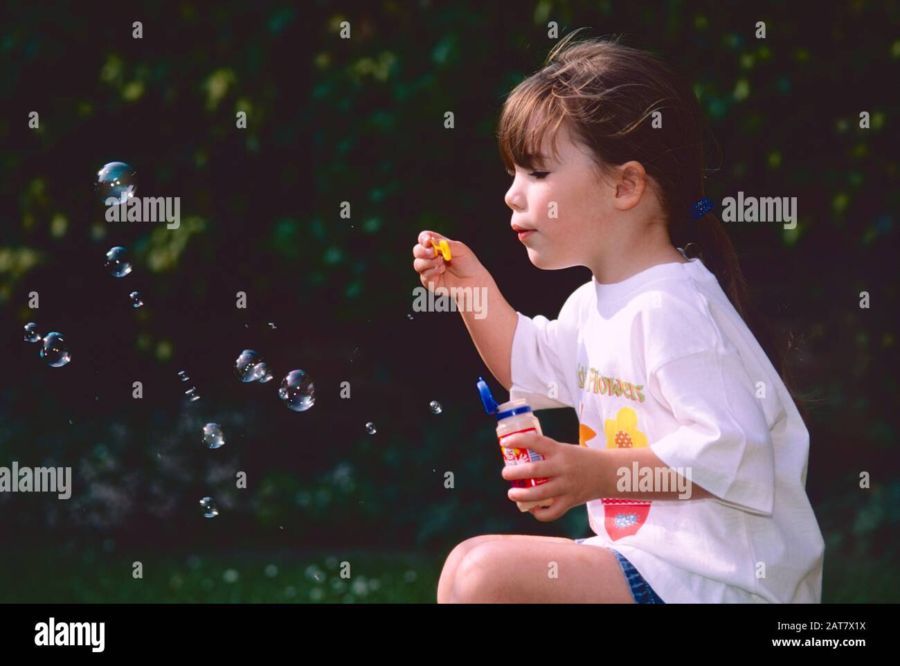 young girl outside in garden blowing bubbles holding pot of bubble ...
