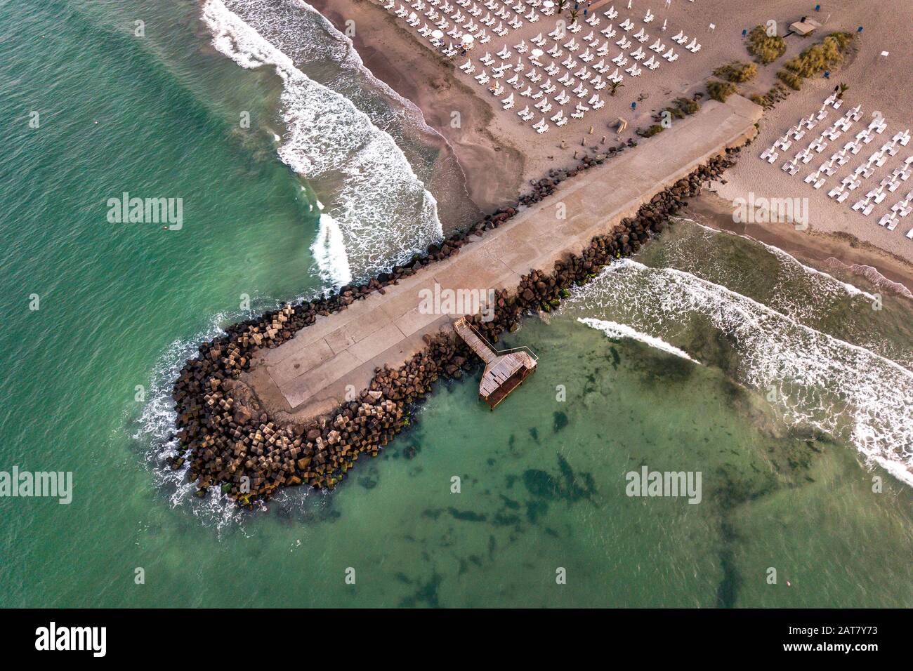 Aerial view of a concrete pier on sea shore with wave breaking stones ...