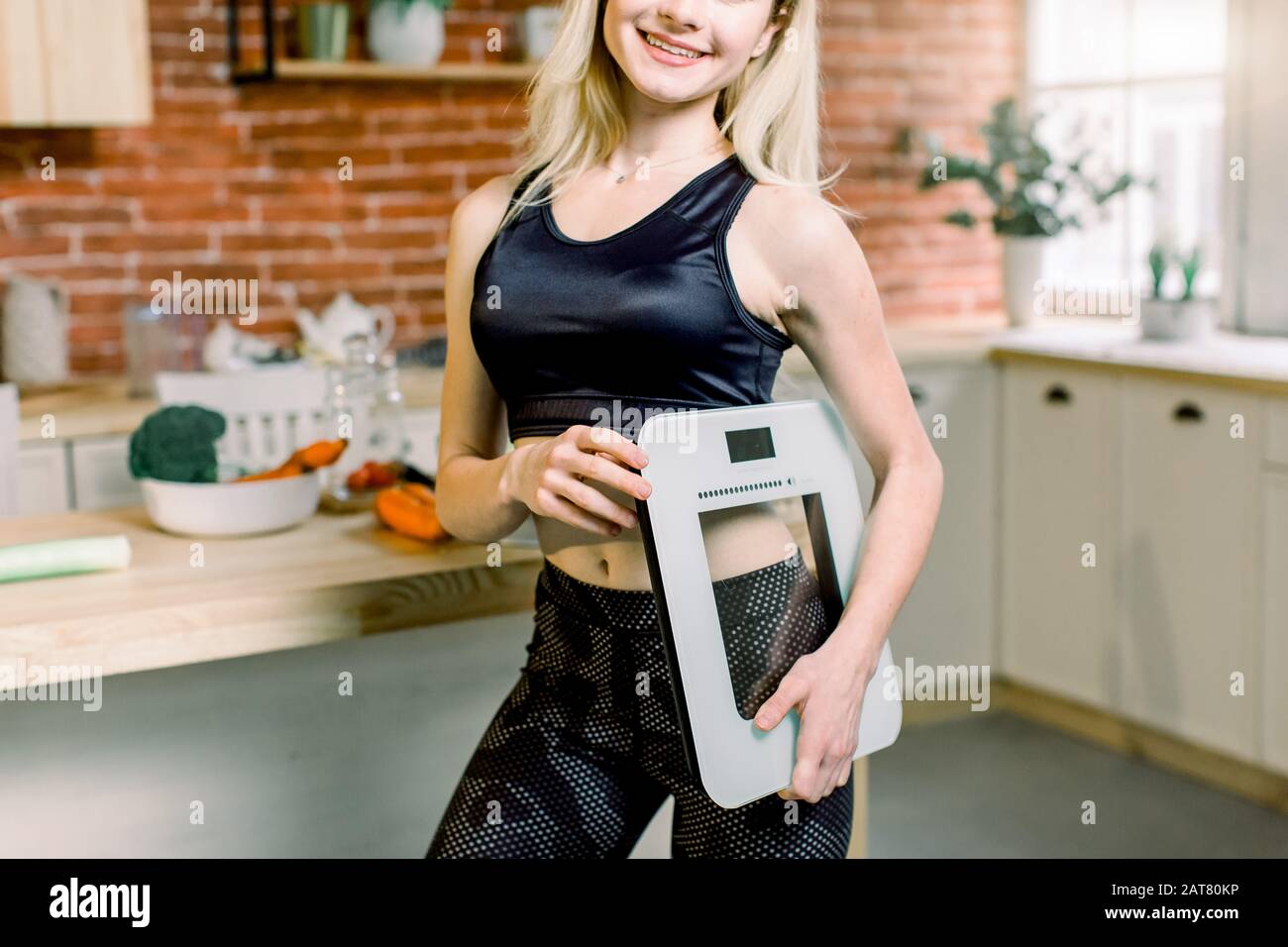 Close-up portrait of beautiful fit woman standing in her kitchen with a ...