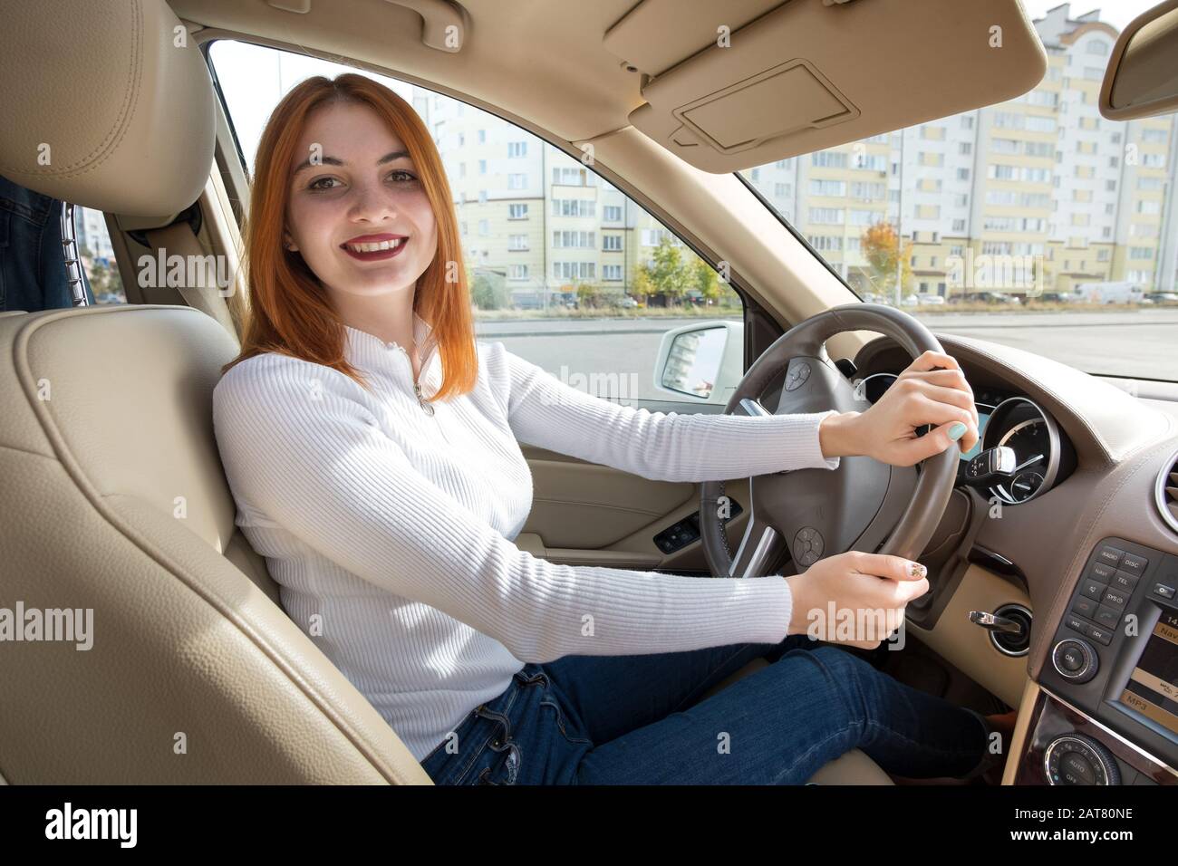 Young redhead woman driver behind a wheel driving a car smiling happily ...