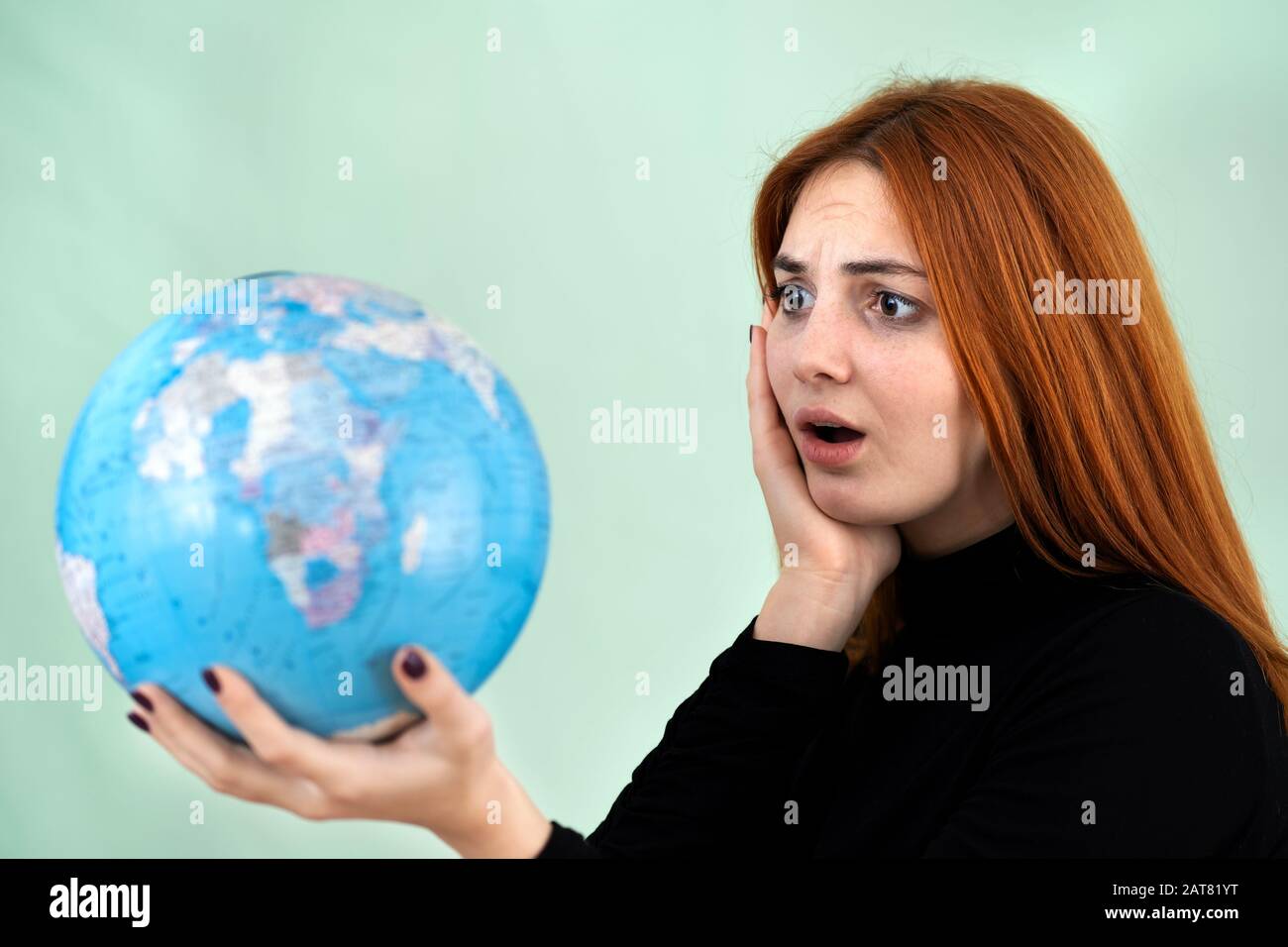 Portrait of a sad worried young woman holding geographic globe of the ...