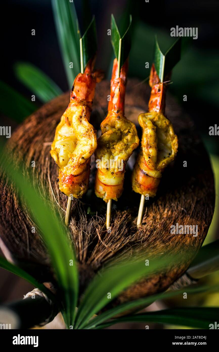 High angle close up of charcoal-grilled prawn satay on a coconut shell ...