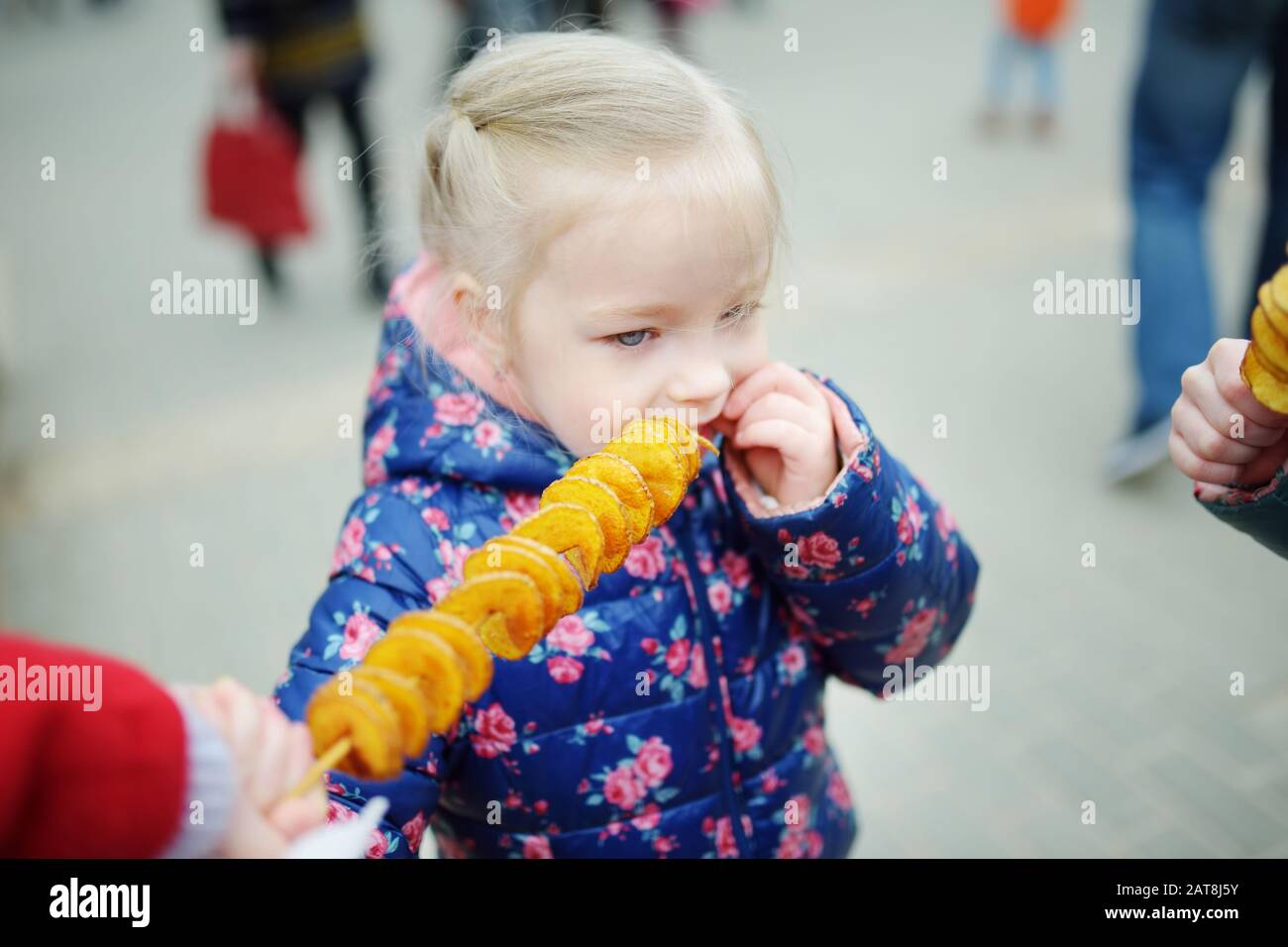 Cute little girl eating fried potato on a stick on cold winter day ...