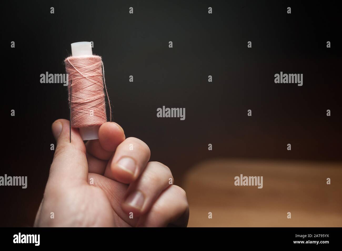 spool of pink thread with a needle in hand on a dark background Stock ...