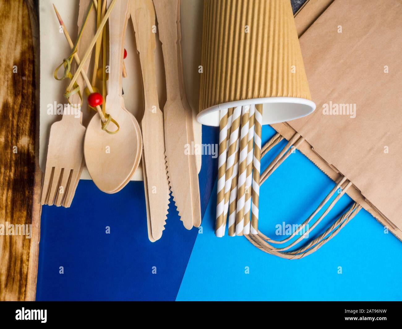 Disposable wooden cutlery and paper bag on trendy blue color background ...