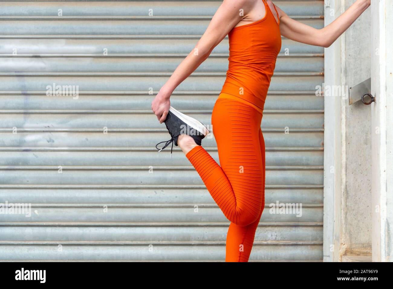 close up of a woman doing leg stretch warm up exercise, wearing orange ...