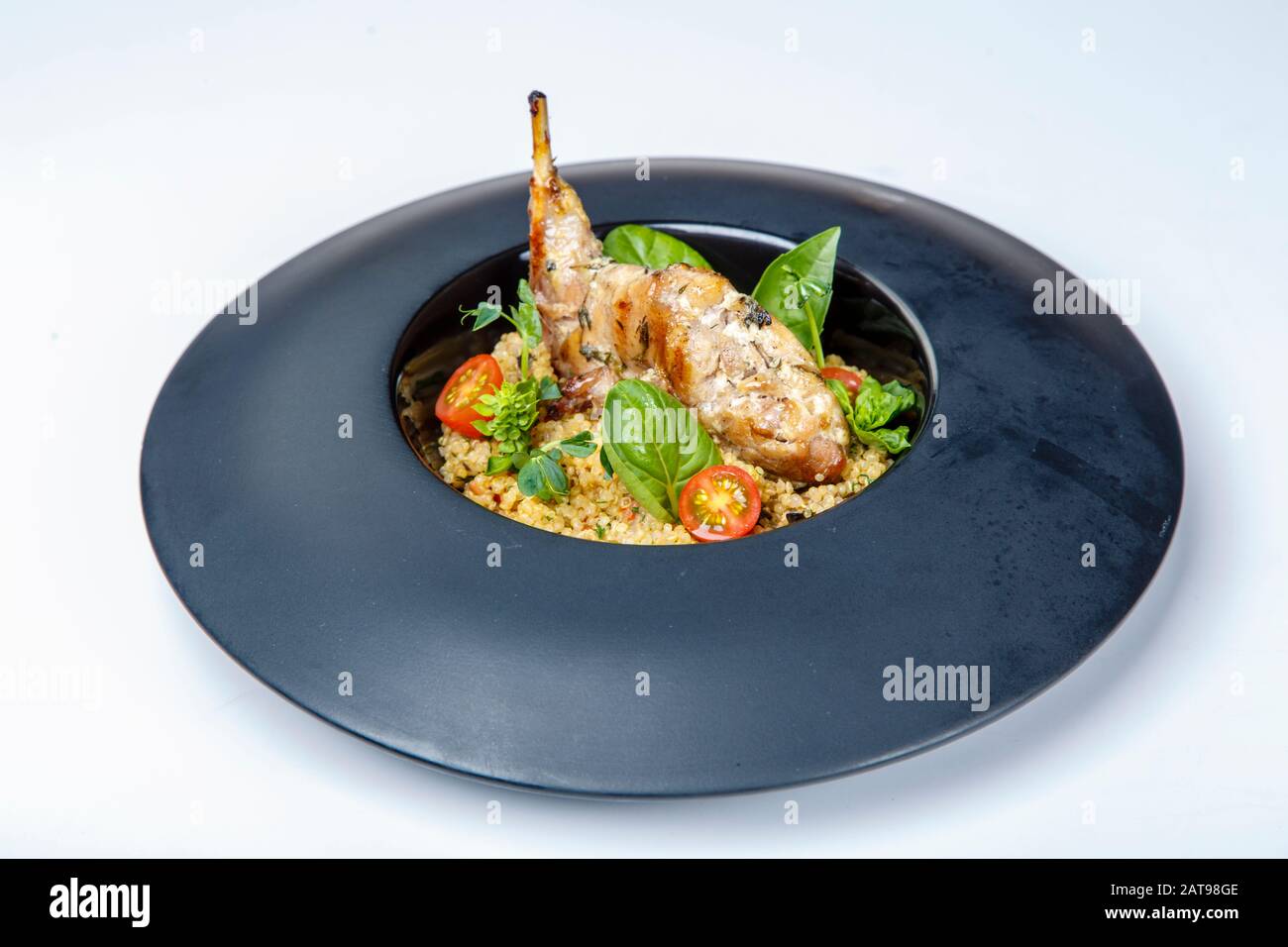Fried rabbit leg with rice on a round black plate. Garnish is decorated ...