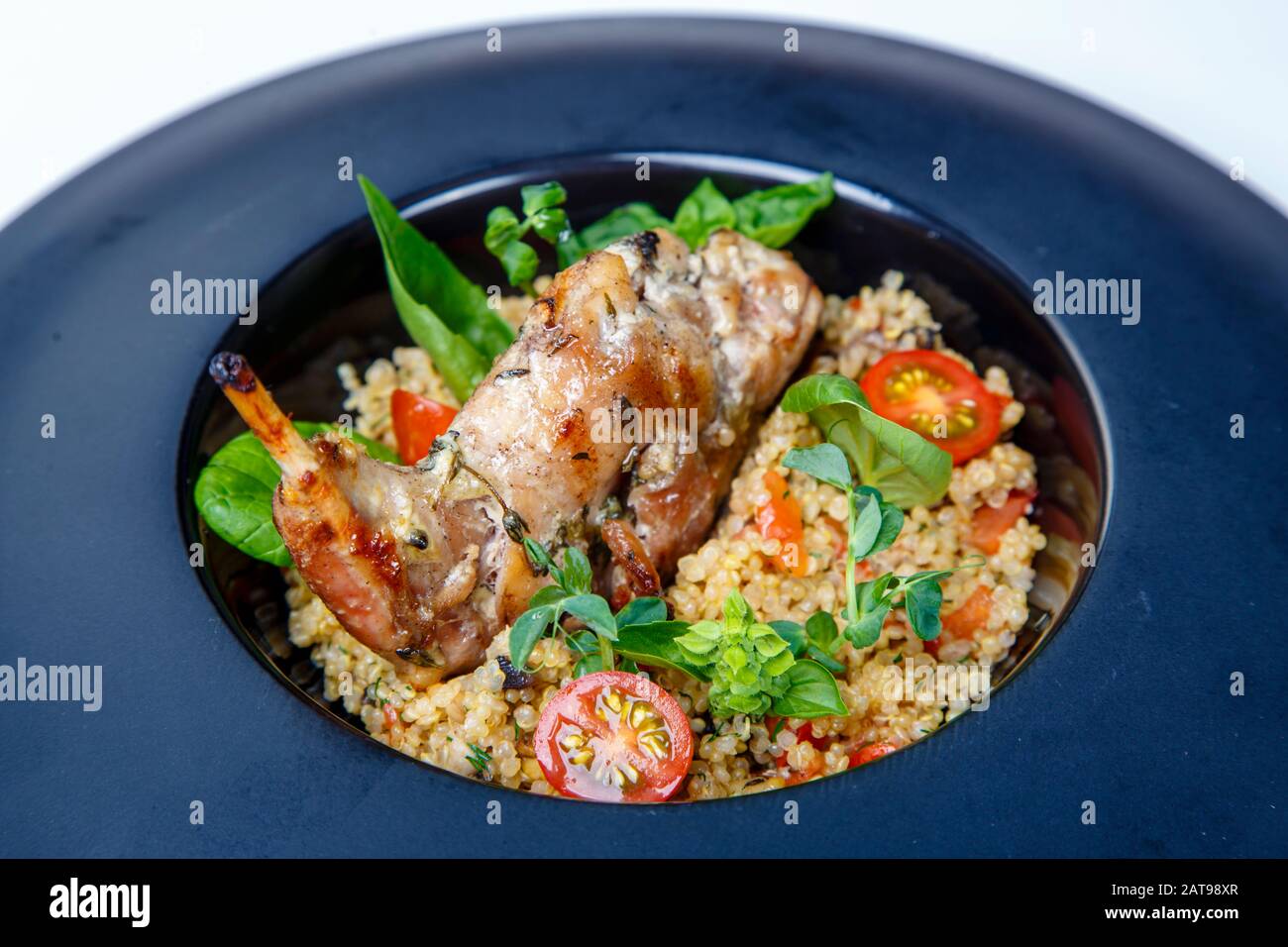Fried rabbit leg with rice on a round black plate. Garnish is decorated ...