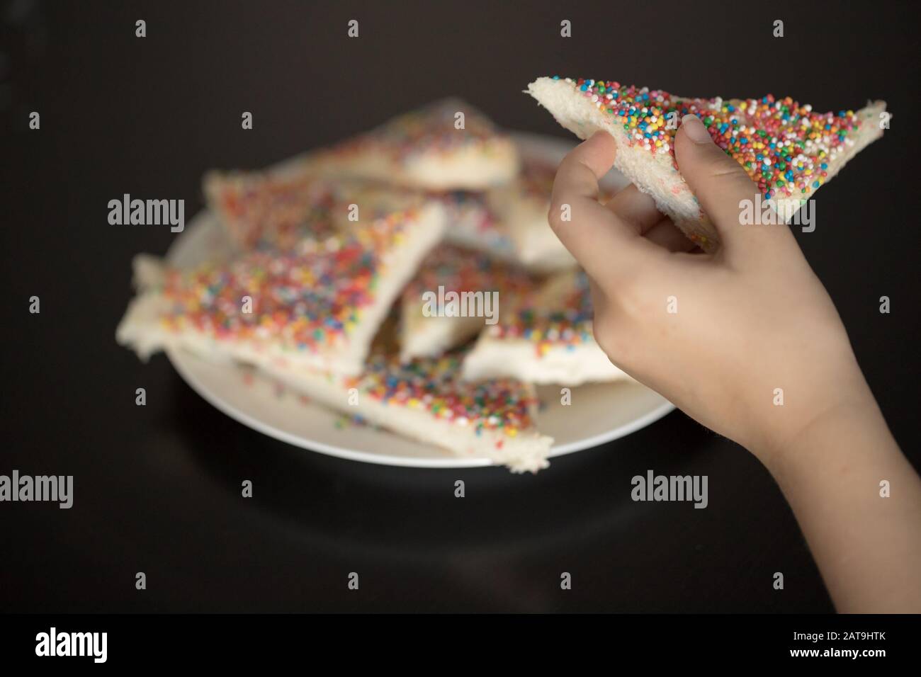 a child's hand taking a piece from a plate of fairy bread, traditional ...
