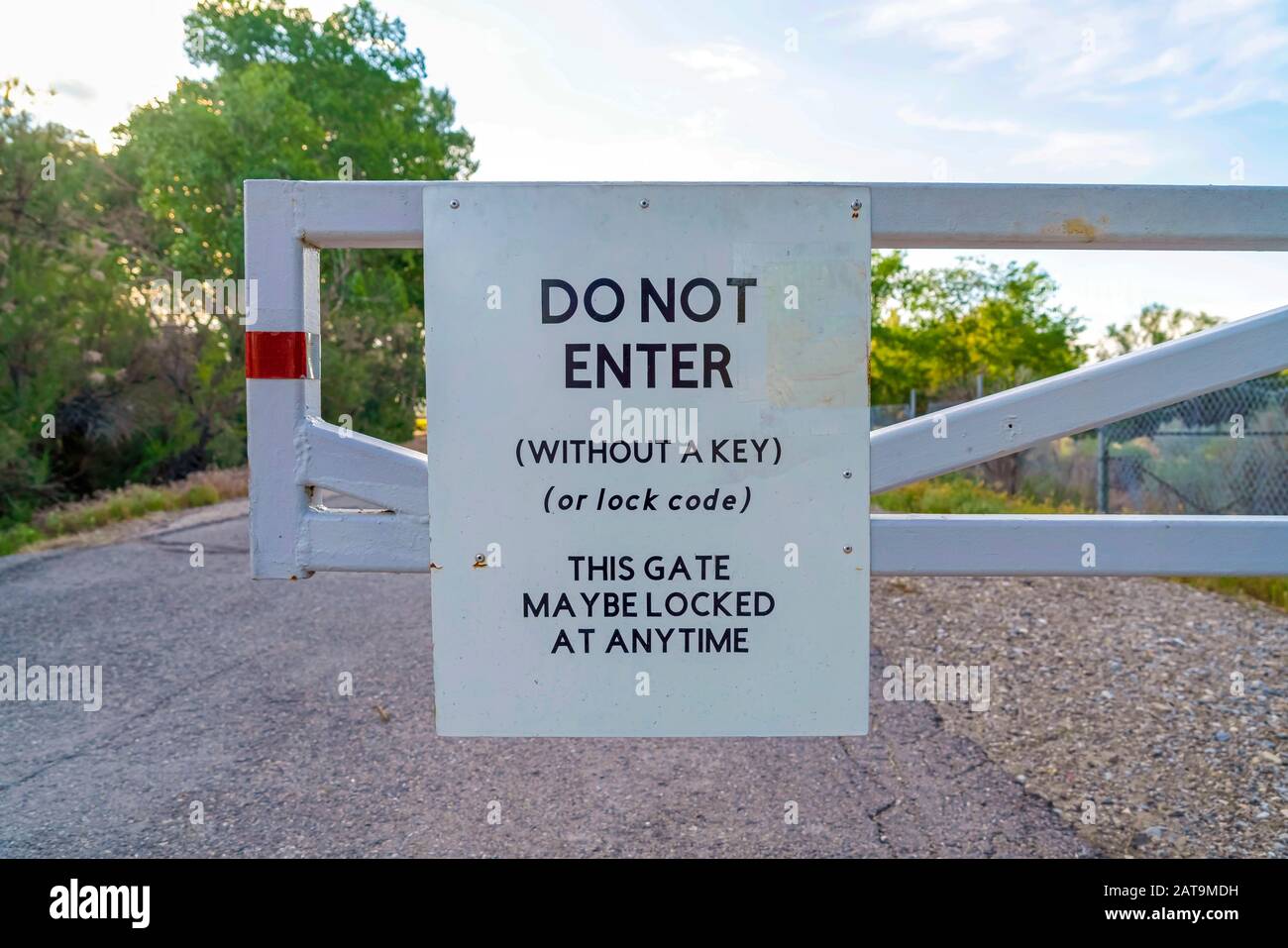 Do Not Enter sign mounted on a white gate against road trees and cloudy ...
