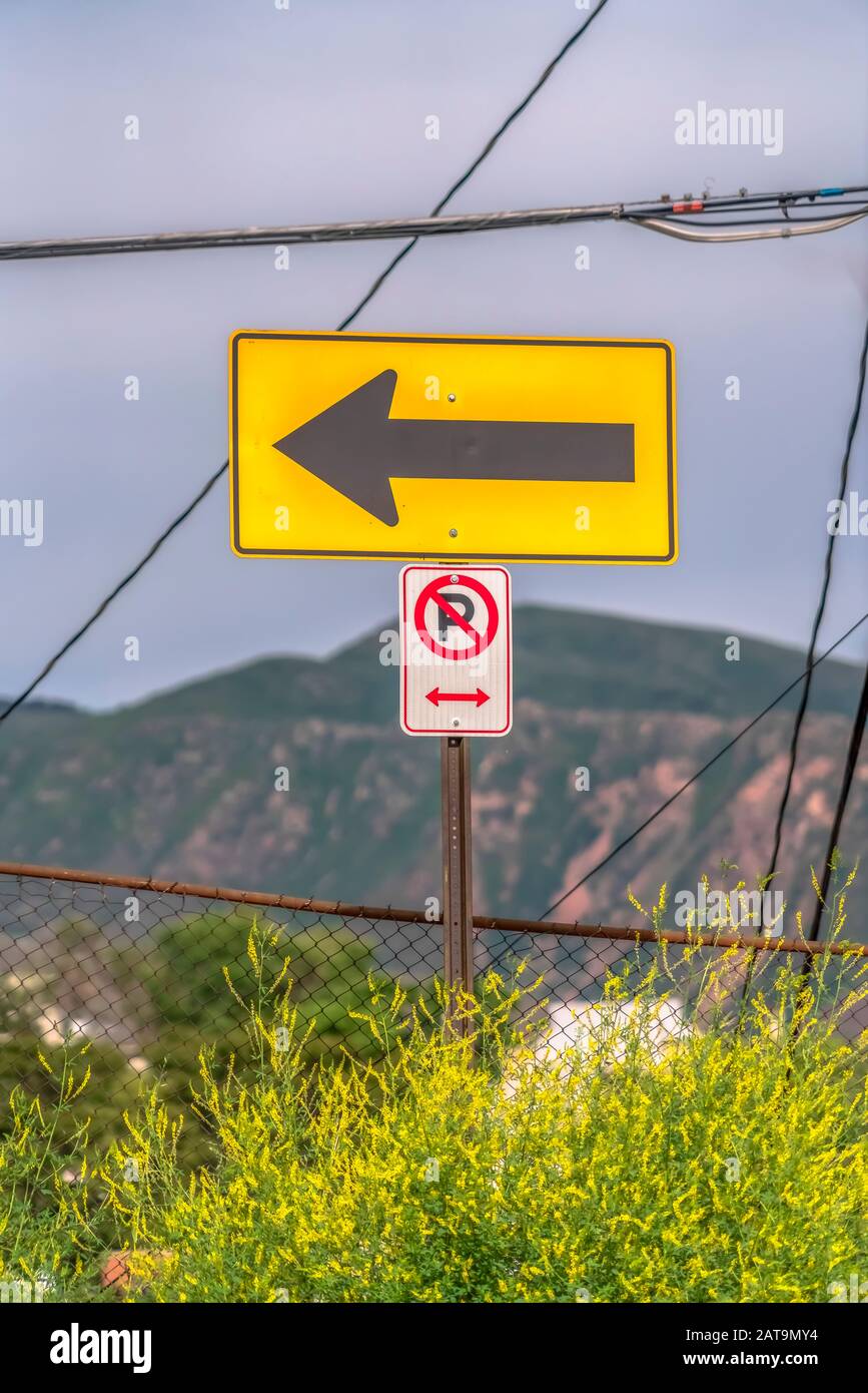No Parking On Both Sides and directional arrow signs against fence and ...