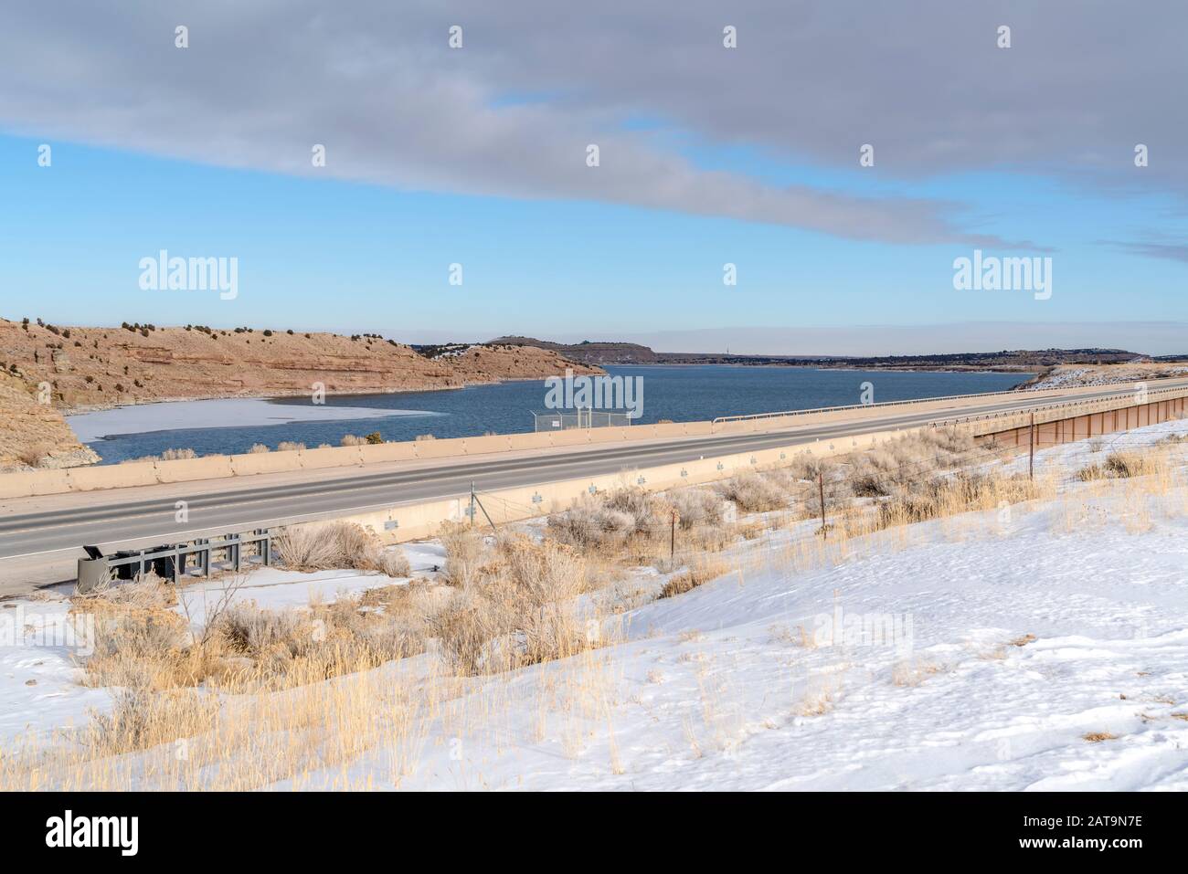 Snow covered terrain along a road overlooking mountain and lake in ...