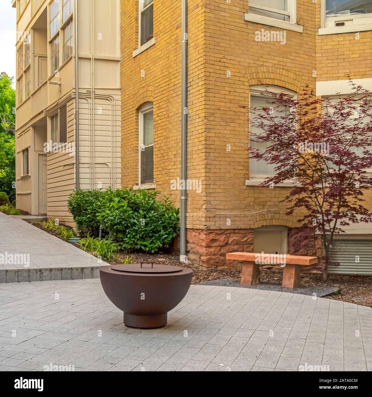 Square Fire pit on circular patio outside building with white and stone ...