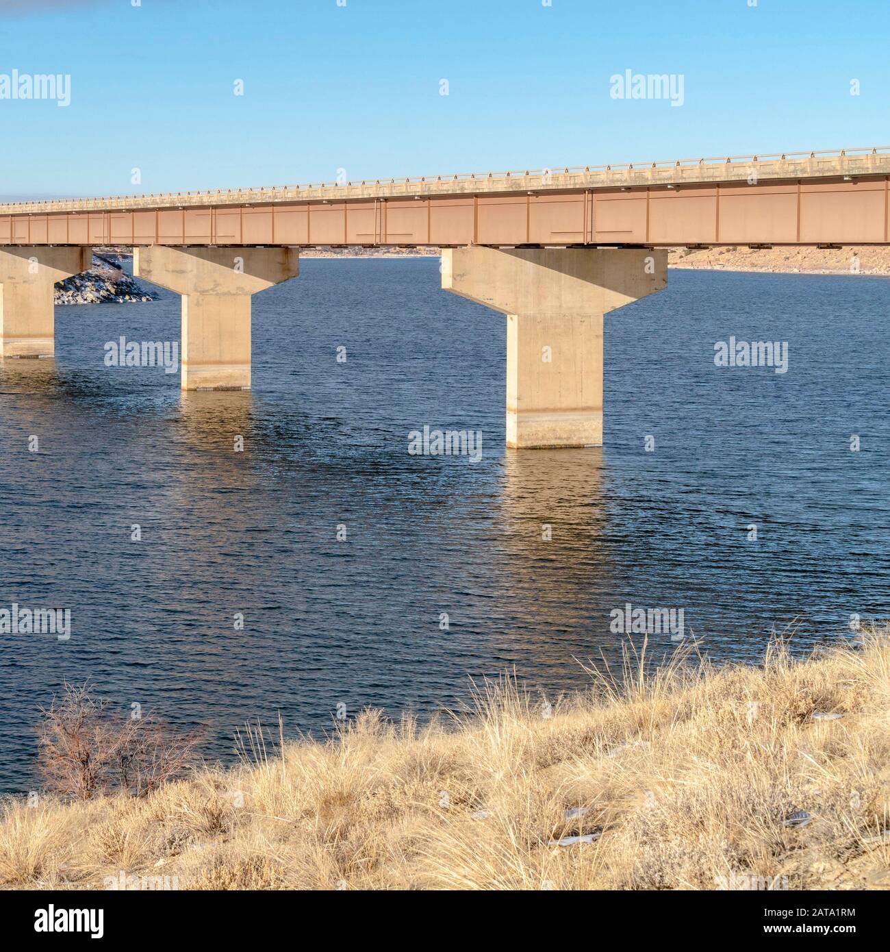 Square frame Bridge across blue lake with views of snow covered hills ...