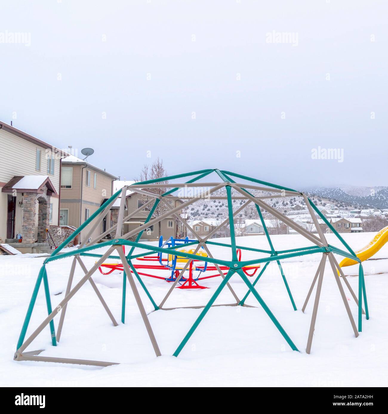 Square Snow covered park with playground against homes hills and cloudy ...