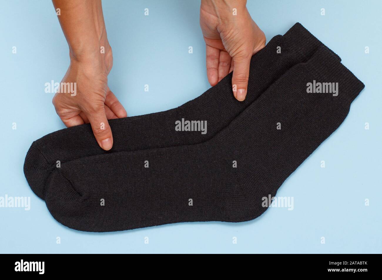 Female hands holding black warm woolen men socks on a blue background ...