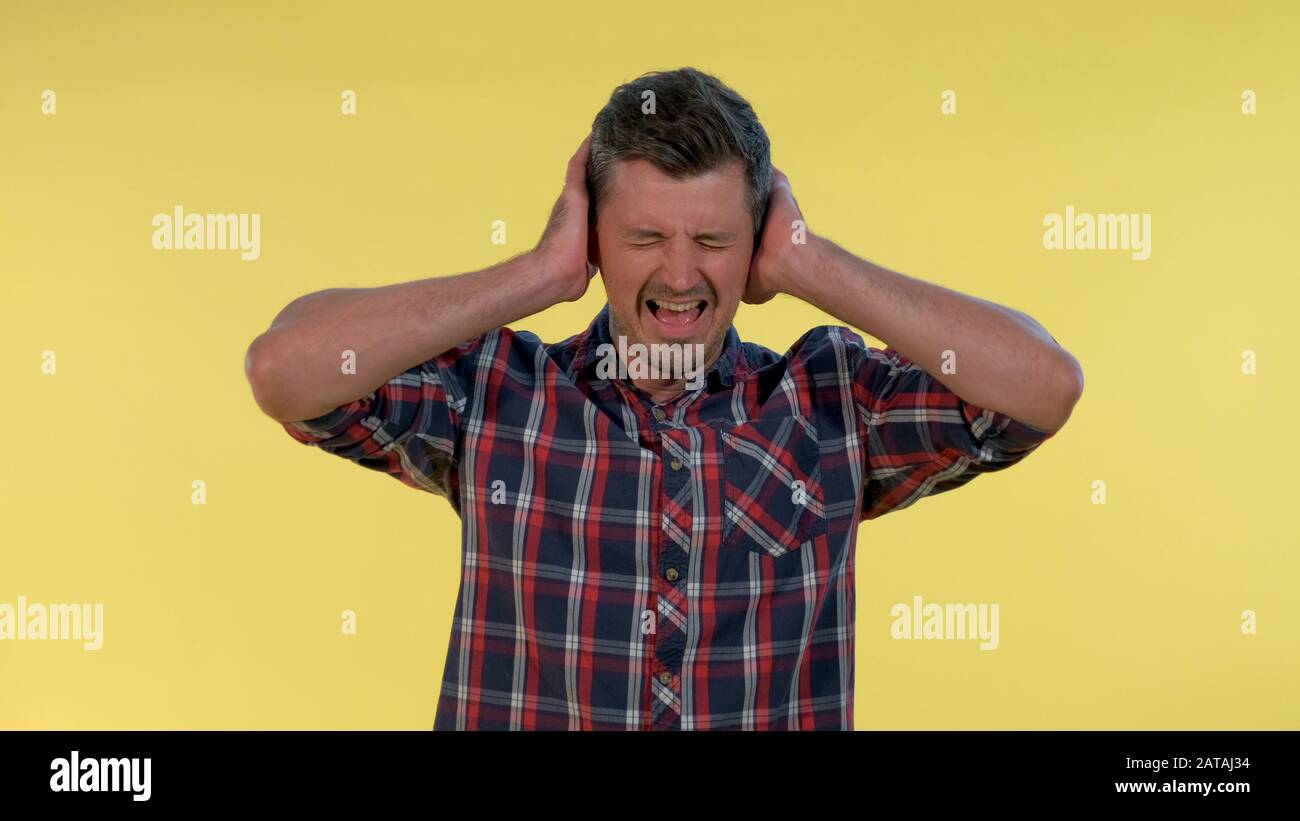 Scared desperate man screaming and covering ears on yellow background ...