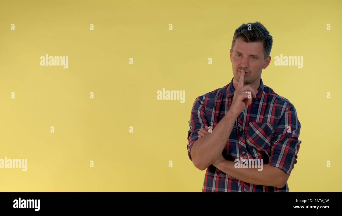 On yellow background cheerful tall boy making a hush gesture. It must ...