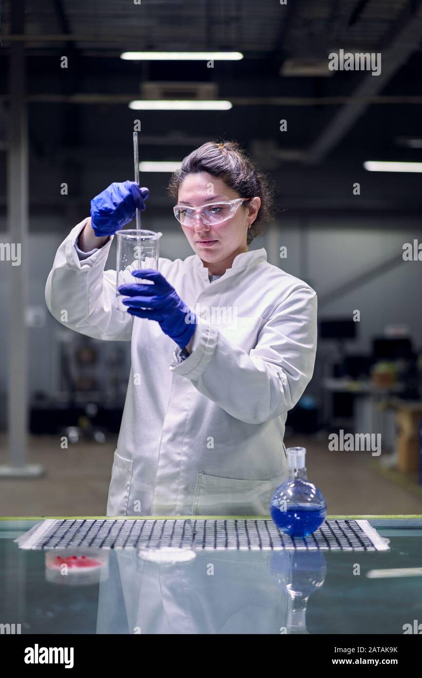 Serious lab girl in glasses and white coat with experimental glass in ...