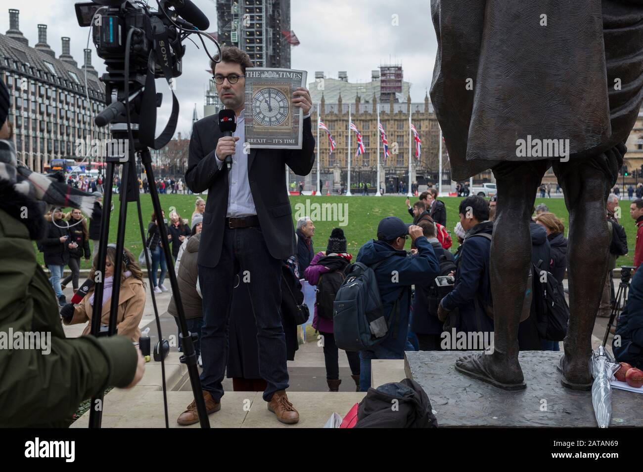 A French TV reporter stands next to the statue of Mahatma Gandhi and ...
