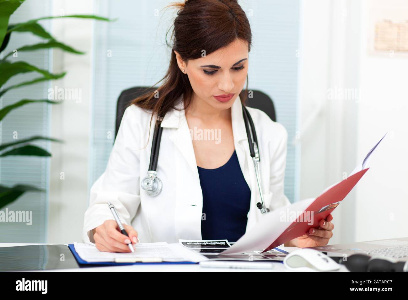 Female doctor reading patient file on clipboard in office desk Stock ...