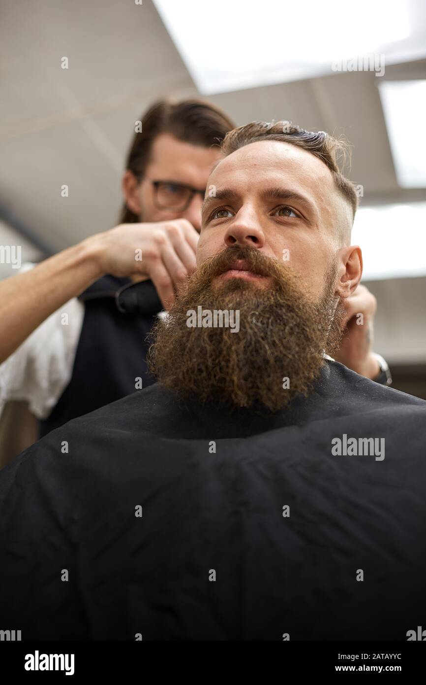 Master cuts hair and beard of men in the barbershop, hairdresser makes ...