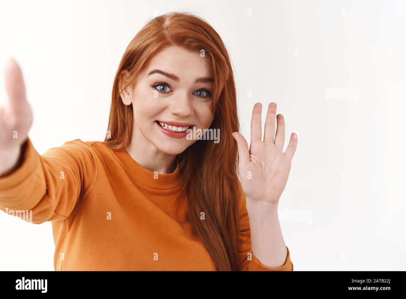 Friendly and outgoing pretty redhead woman in orange sweater, extend ...