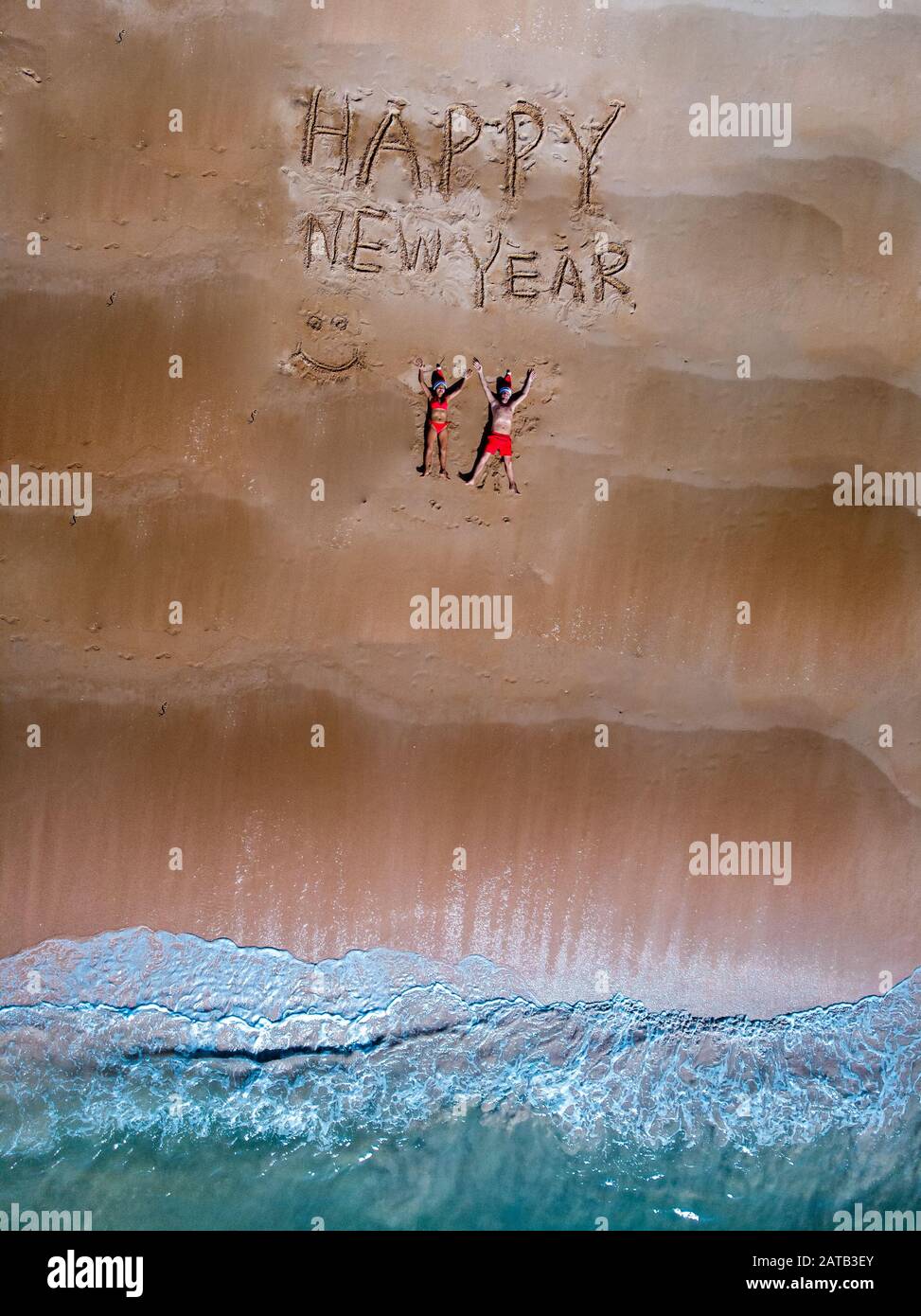Happy new year sign on the beach with couple in the sand and chritmas ...