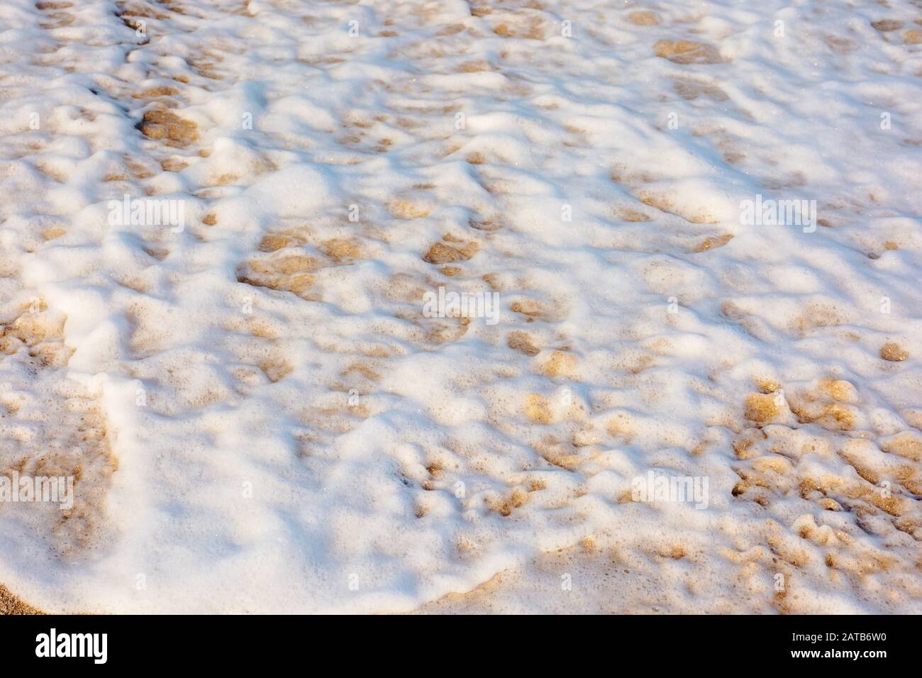 sea waves splash foam on the sunny beach. mess of salt water and sand ...
