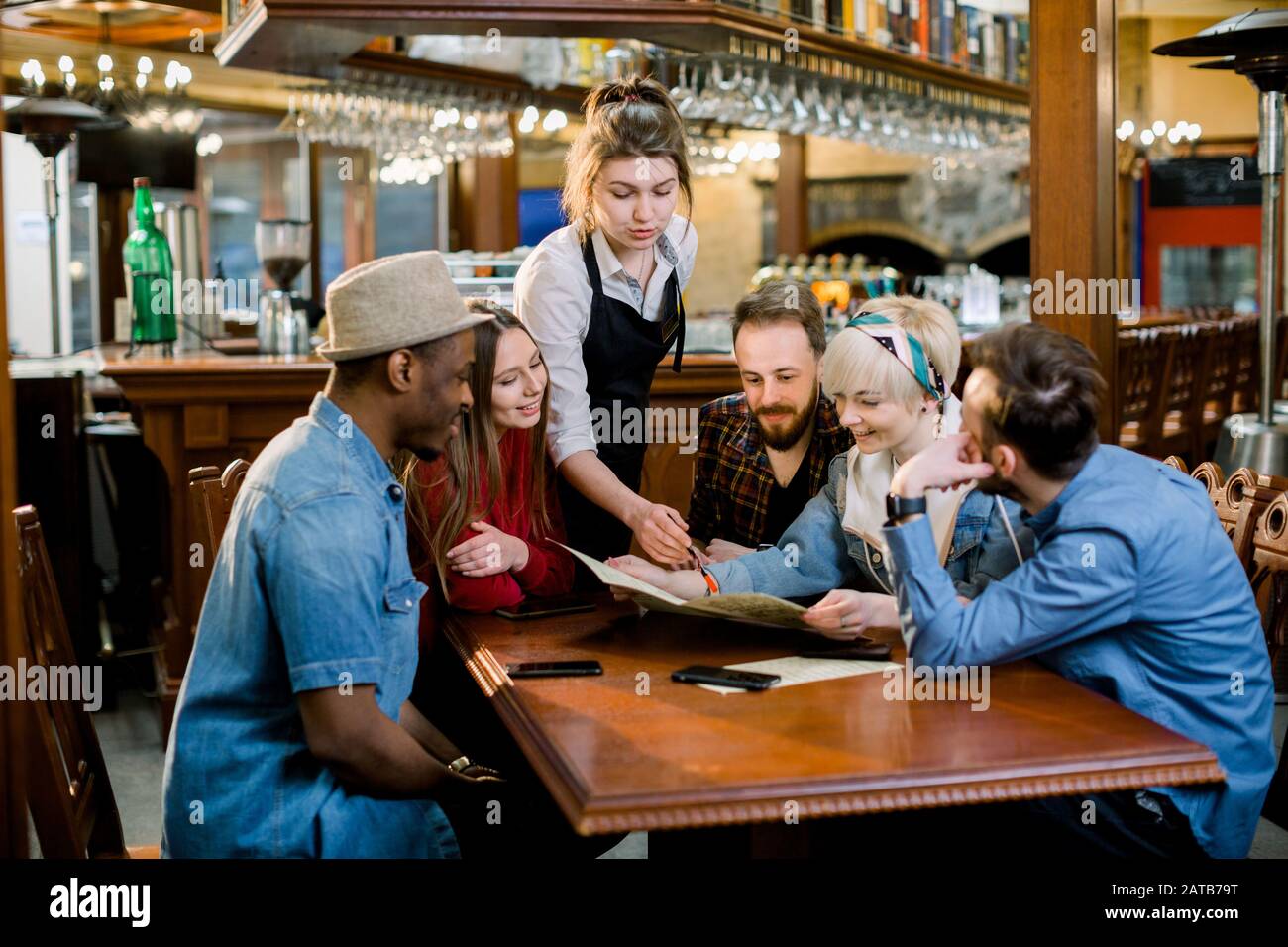 Group of diverse young friends sitting together at a table in a trendy ...
