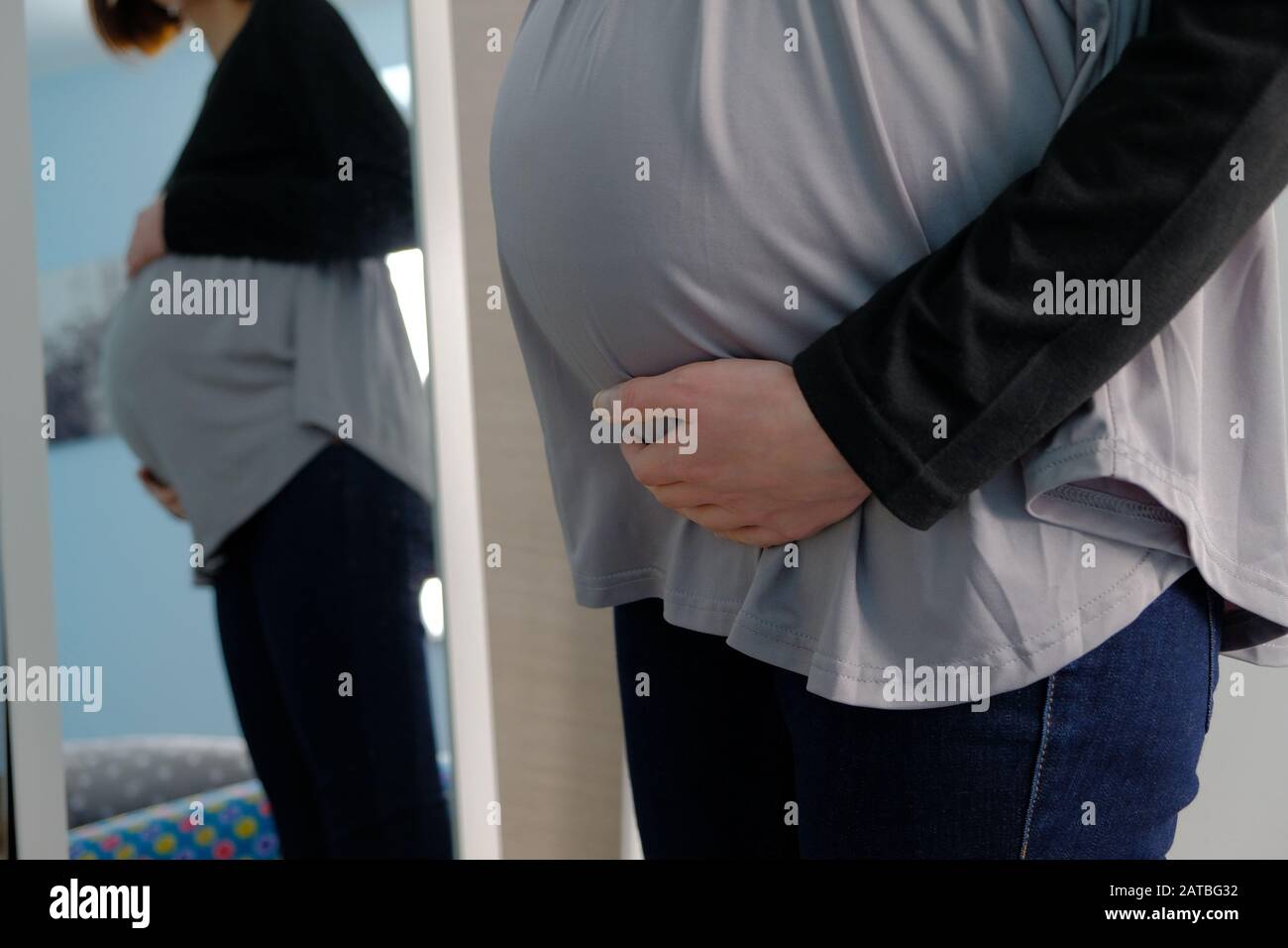 A young Caucasian woman looks at her belly in the mirror during ...