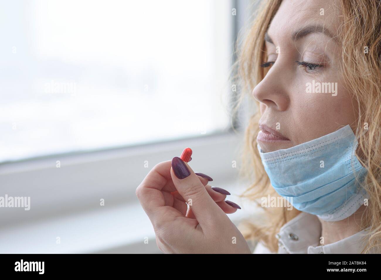 A Mature, thoughtful, blond woman with a pill in her hand. Medical mask ...