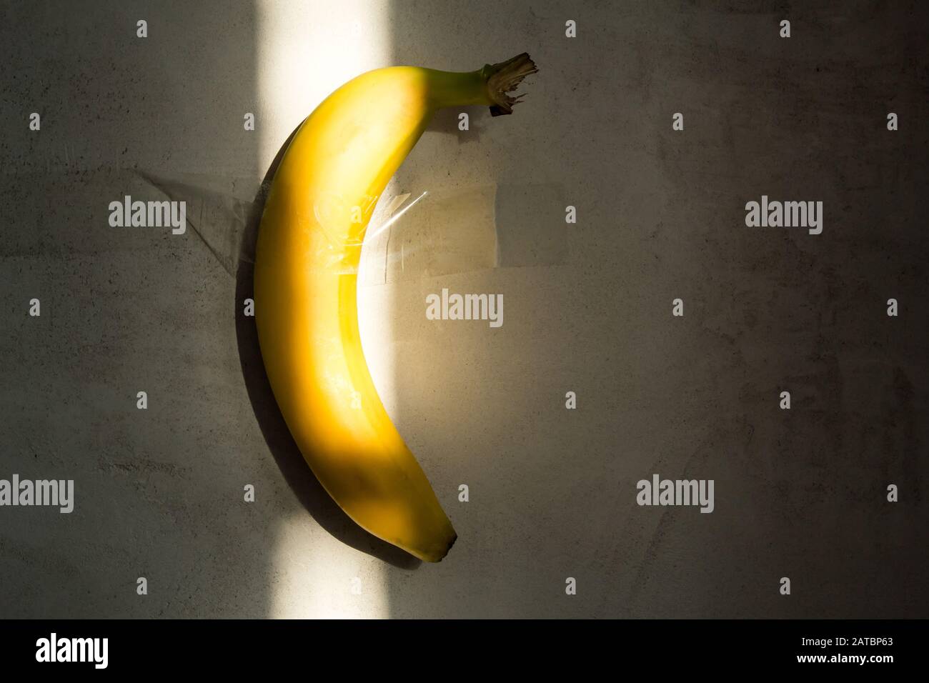 Yellow banana hanging on a concrete wall with a ray of sunlight. A ...