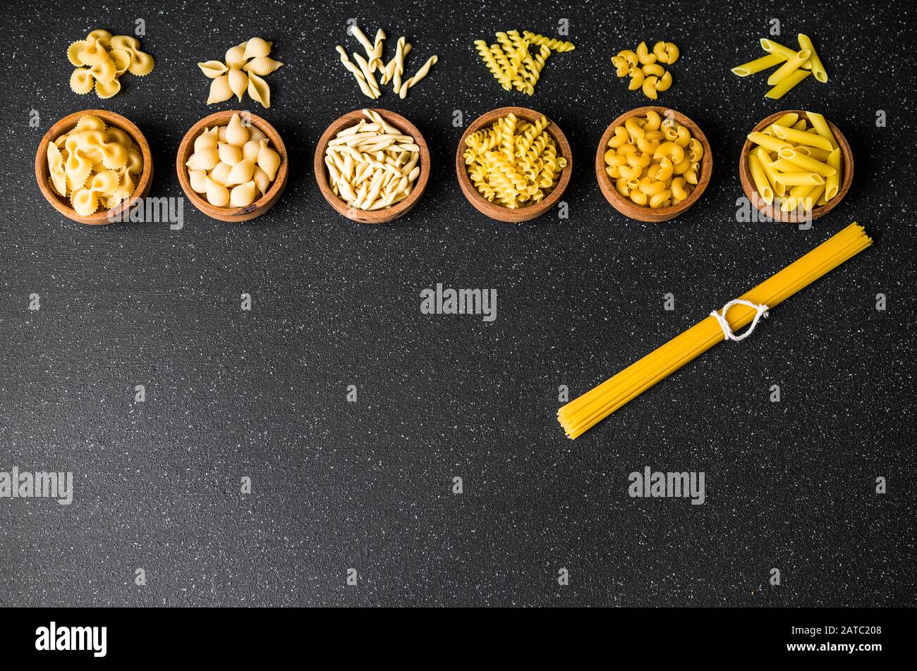 Assortment of different dry pasta types against black background, top ...