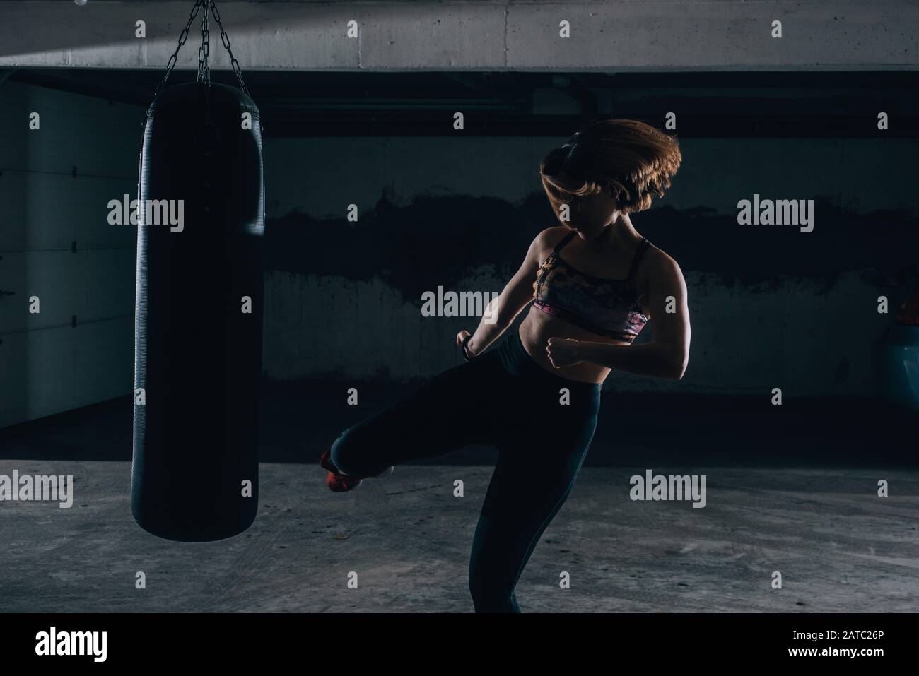 Young silhouette female practicing high kick with the boxing bag inside ...