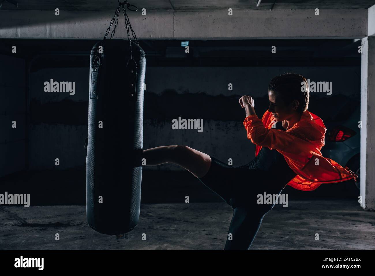 Young silhouette female practicing high kick with the boxing bag inside ...