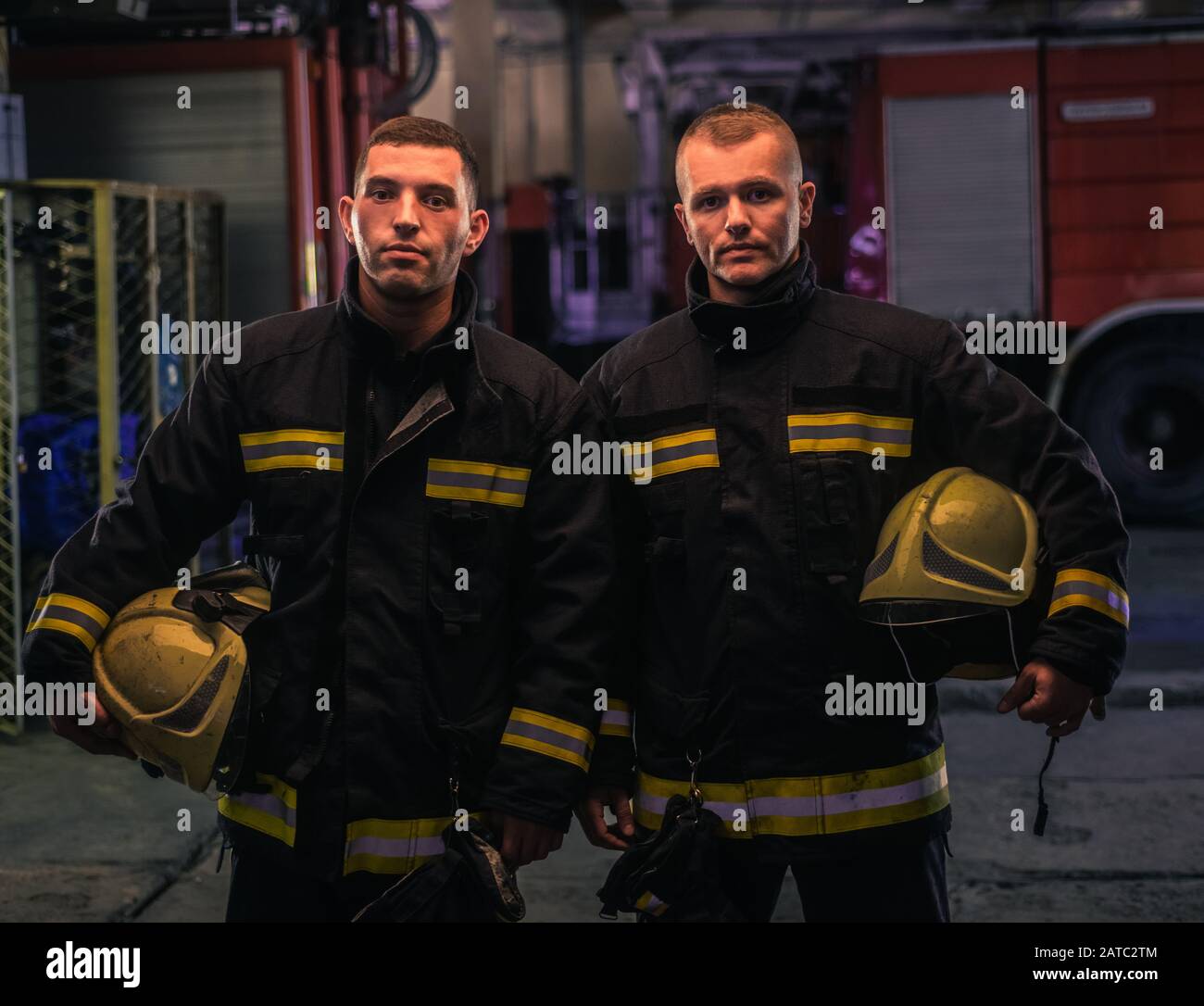 Portrait of two young firemen in uniform standing inside the fire ...