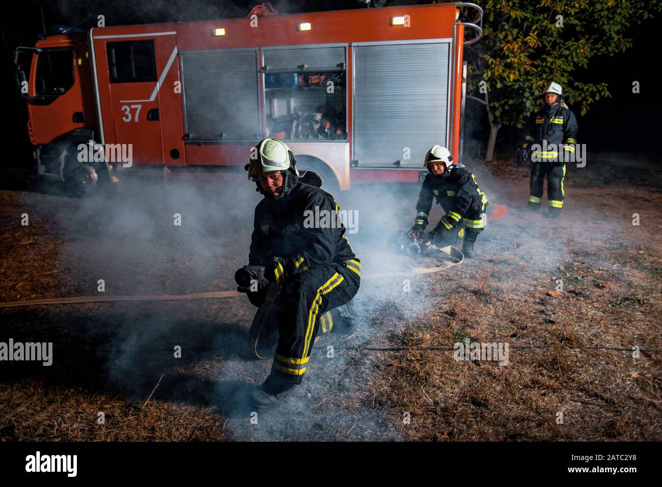Group of firemen putting out a fire with a long water hose Stock Photo ...